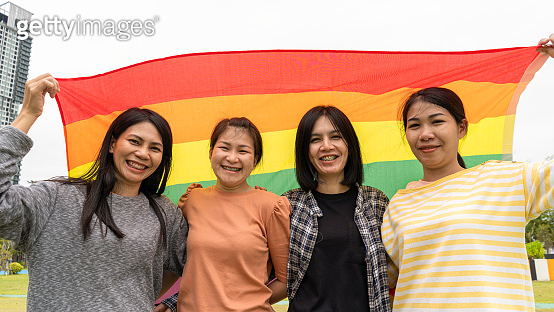 Lesbian and gay 3 people hugging outdoors. LGBT hugging by rainbow flag ...