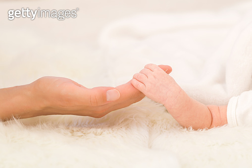Baby hand clinging young adult mother finger on white soft fur blanket ...