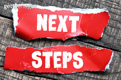 NEXT STEPS words on small red sheets of paper laid on a wooden table ...