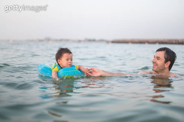 Cute baby boy swimming in the seaside wearing a float with his father ...