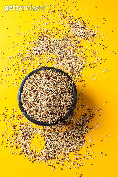 Different types of quinoa grains in black marble bowl on yellow ...
