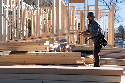 Construction Worker Moving Lumber with Framed House in Background ...