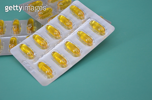 Yellow Omega 3 capsules in blisters lying in a row on a green ...