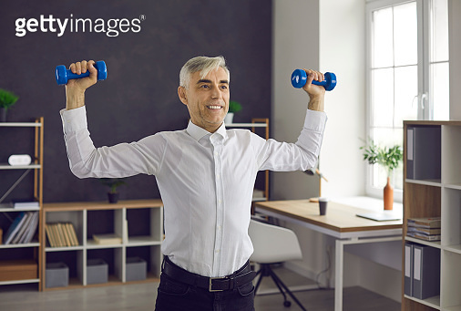 Happy senior worker doing fitness exercise during working day in office ...