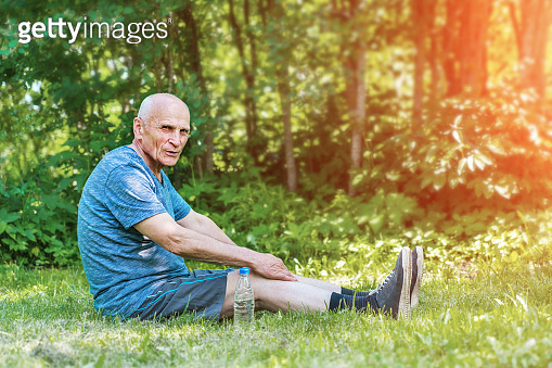 Old man seated on park lawn surface is exercising lean and stretching ...