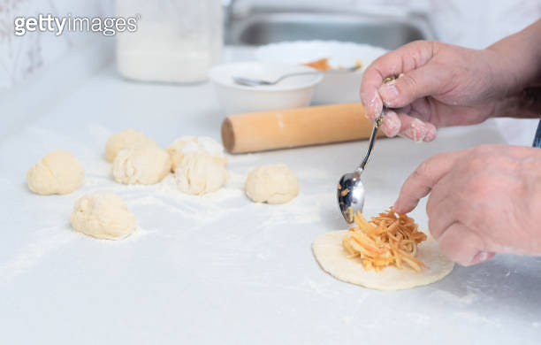 Senior woman hands put the apple filling on the dough for pies on a ...