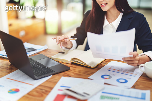 Asian female worker using computer and budget documents on desk ...