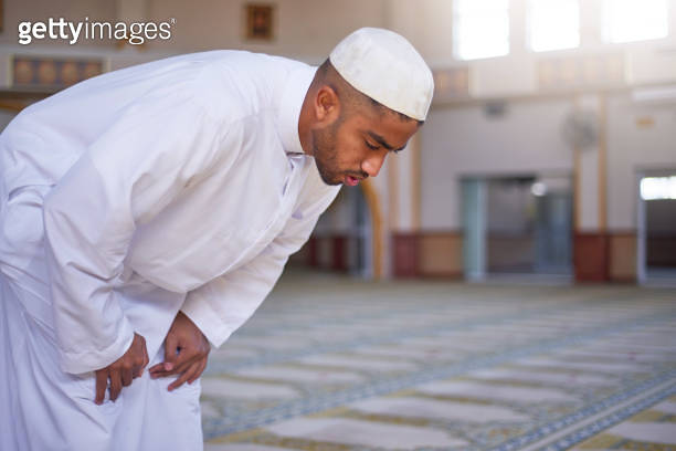 A side close view of a young Muslim man bowing during prayers at a ...