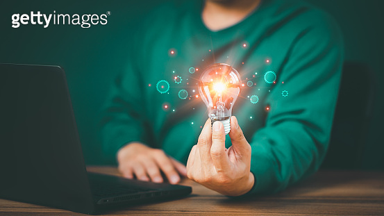 Man holding a light bulb while working on the computer to think and ...