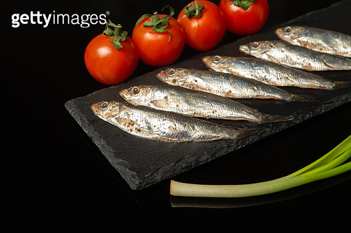 Sprat with vegetables on a serving black board. Small salted fish with ...