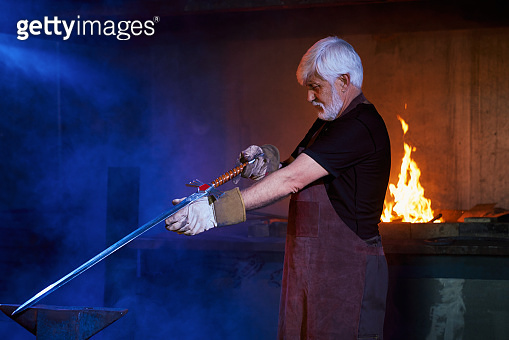 Competent aged blacksmith making sword at forge (1366635068) - 게티이미지뱅크