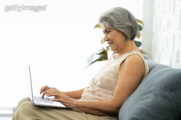 Happy older mature mother typing laptop computer while sitting on sofa ...