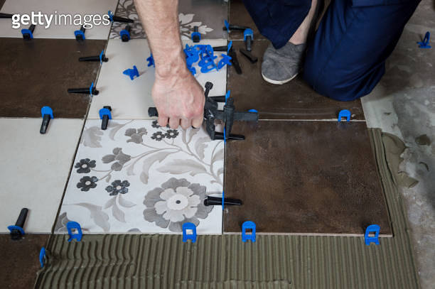 The worker puts the ceramic tile on the floor, clamps the clamps with ...