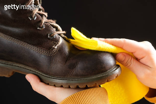 A woman cleans brown nubuck boots on a black background, wipes the dust ...