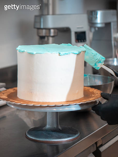 cake designer covering a frosted blank cake with turquoise light blue ...