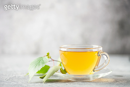 Glass cup of hot, fragrant birch tea on a grey background and a branch ...