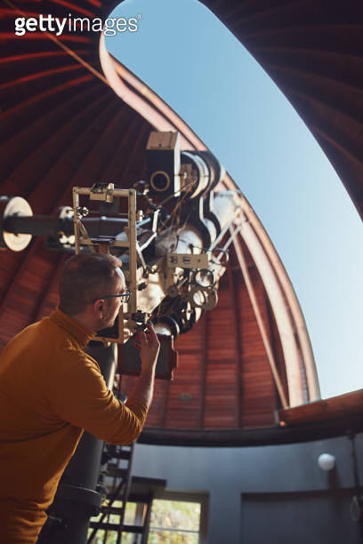 Astronomer with a big astronomical telescope in observatory doing ...