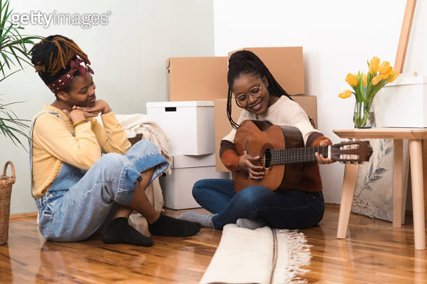 Two African roommates playing a guitar and relaxing while moving in ...