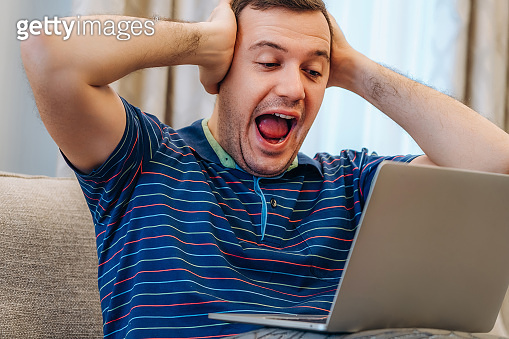 Surprised attractive man using internet on his laptop looking excited ...