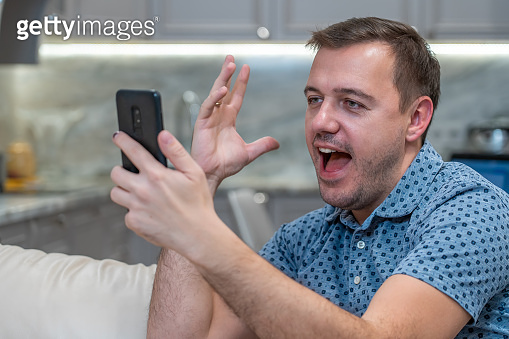 Joyful millennial man sitting on couch, reading sms with good luck news ...
