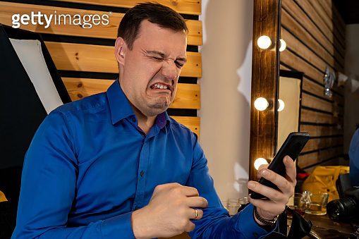 Annoyed millennial man with disgust look at smartphone screen indoors ...
