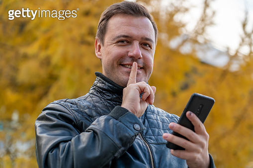 Portrait of mysterious attractive guy using gadget showing shh sign in ...