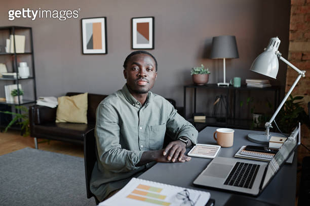 Horizontal portrait of handsome young Black man sitting at desk in ...