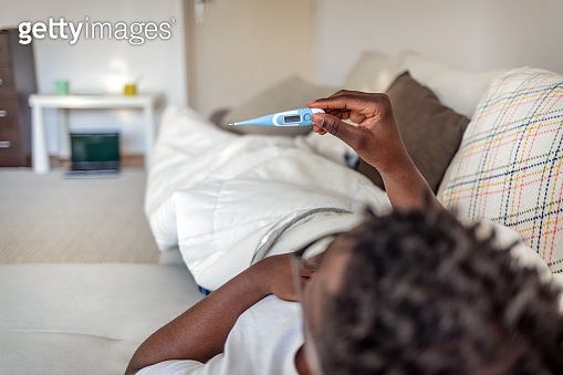 Young sick african guy with fever, checking body temperature with ...