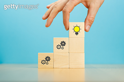 Hand putting wooden block pyramid with gears and light bulb icons on blue background. 이미지 ...