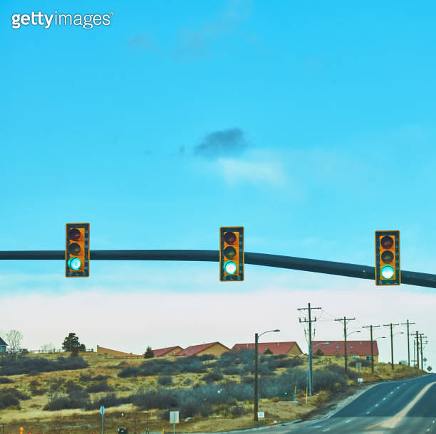 Traffic lights on an overhang with road and homes visible. Summer day ...