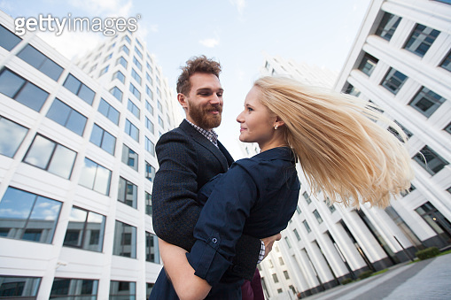 Man and woman hugging and laughing in front of a white building. Bottom ...