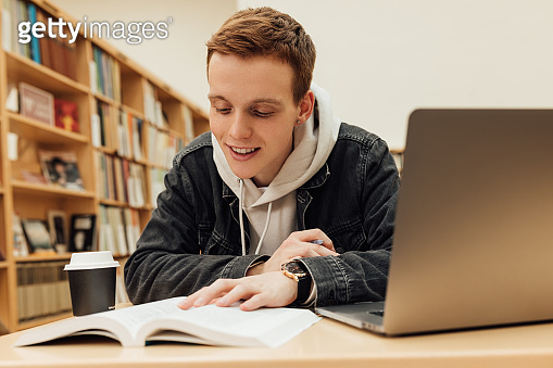 Smiling student with ginger hair preparing exams in library. Student ...
