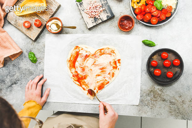 Hands of a caucasian teenage girl in an apron smear tomato sauce on a ...