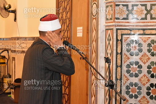 A mosque Imam preacher muezzin in front of the microphone reciting ...
