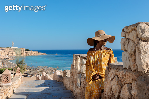 Happy African American woman in yellow dress and sun hat enjoys view of ...