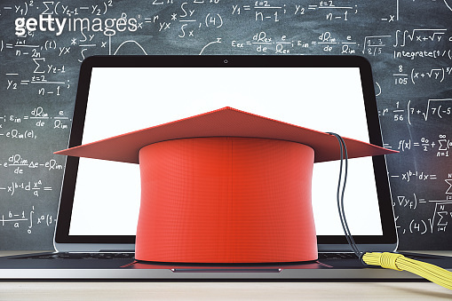 Close up of red graduation cap on open laptop and chalkboard wall ...