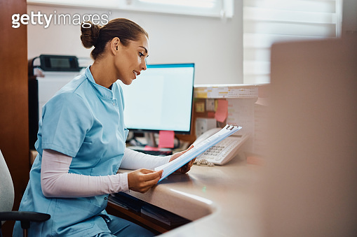 Young nurse going through medical records at reception desk in the ...