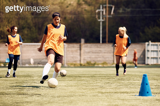 Sportswoman leading the ball around cones during soccer training on ...