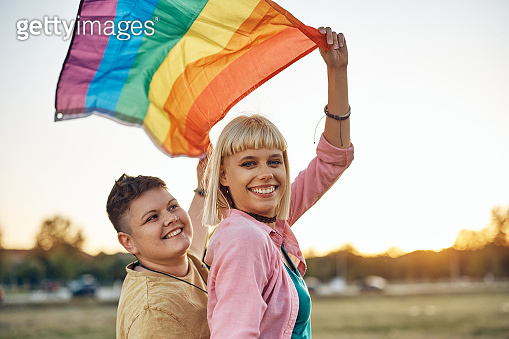 Carefree female couple with LGBT flag having fun together in nature ...