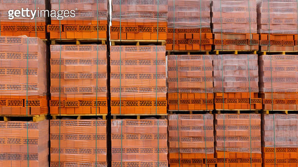 Red brick packed in stacks are stored on ground outdoors at a hardware ...