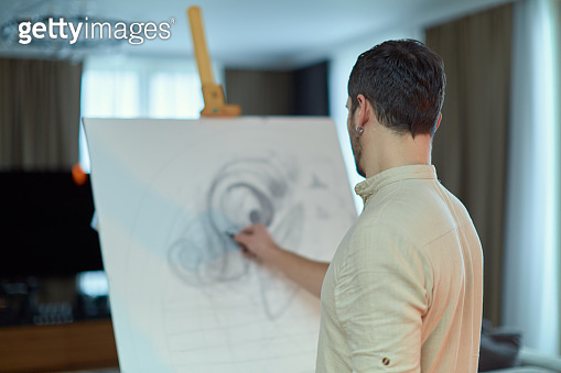 Guy drawing on canvas at easel at home. Talented man creating draft ...