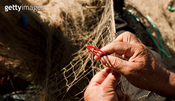 fishing net in the hands of fisherman, he weaves and repairs by sewing ...
