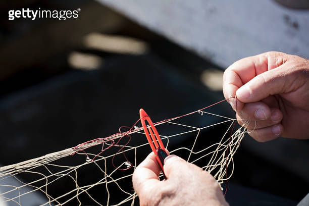 fishing net in the hands of fisherman, he weaves and repairs by sewing ...