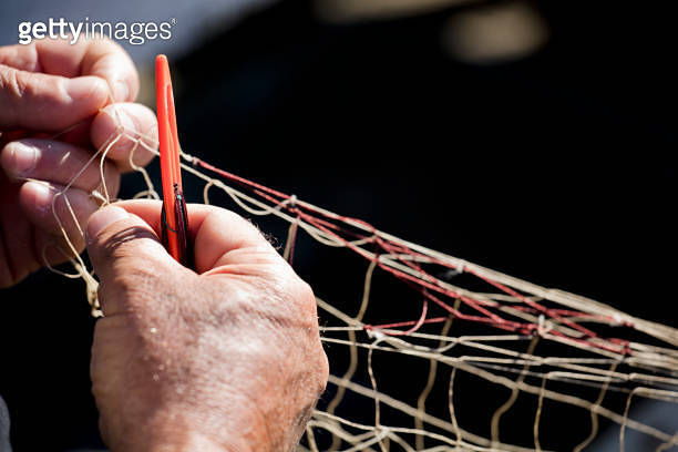 fishing net in the hands of fisherman, he weaves and repairs by sewing ...