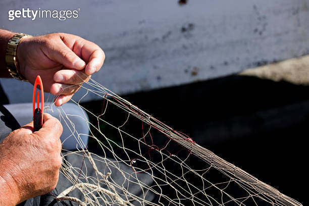 fishing net in the hands of fisherman, he weaves and repairs by sewing ...
