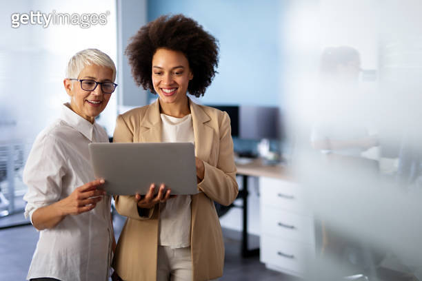 Happy multiethnic business women working together online on a laptop in corporate office ...