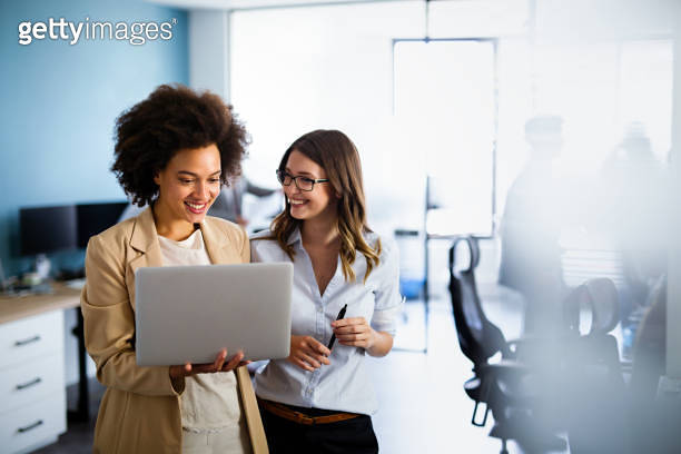 Happy multiethnic business women working together online on a laptop in corporate office ...