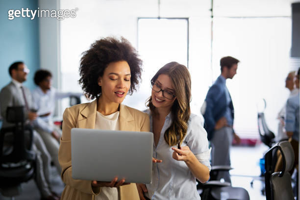 Happy multiethnic business women working together online on a laptop in corporate office ...