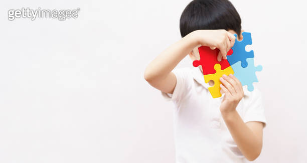 Young small Asian boy holding colorful jigsaw puzzle up cover his face ...