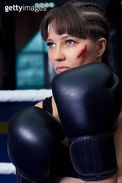 Female fighter with boxing gloves on her hands stands in a boxing ring ...